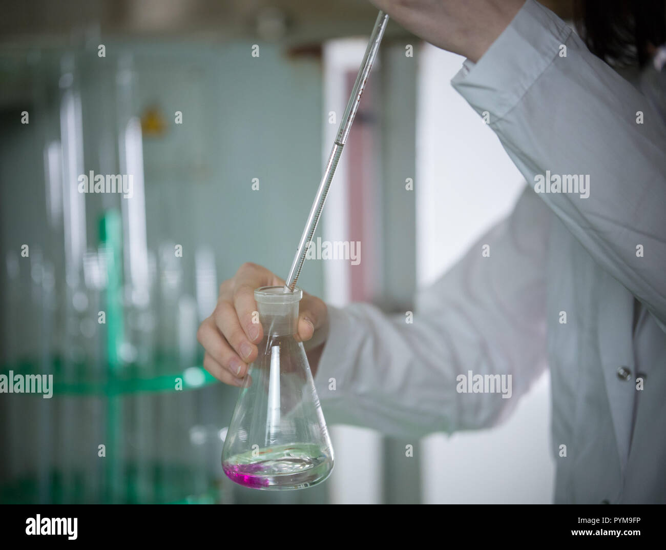 Chemical laboratory. Young woman holding a flask, dripping something ...