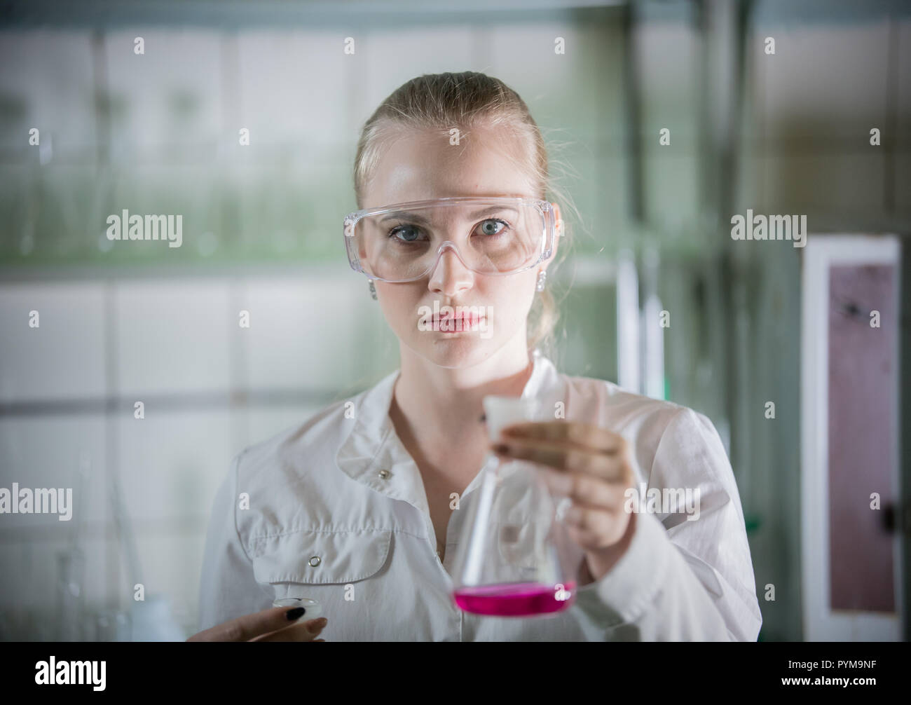 Chemical laboratory. Young blonde woman holding a flask with liquid in ...