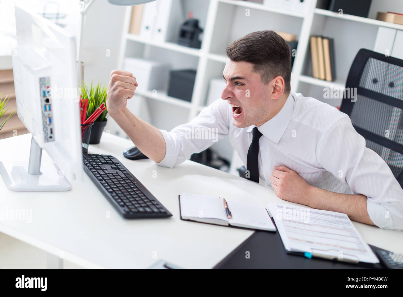 A young man sitting at a computer Desk in the office and shows his fist ...