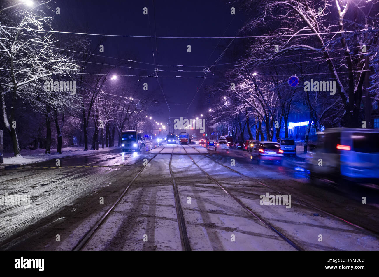 Center of the snowy road with trams. The night city with night traffic ...