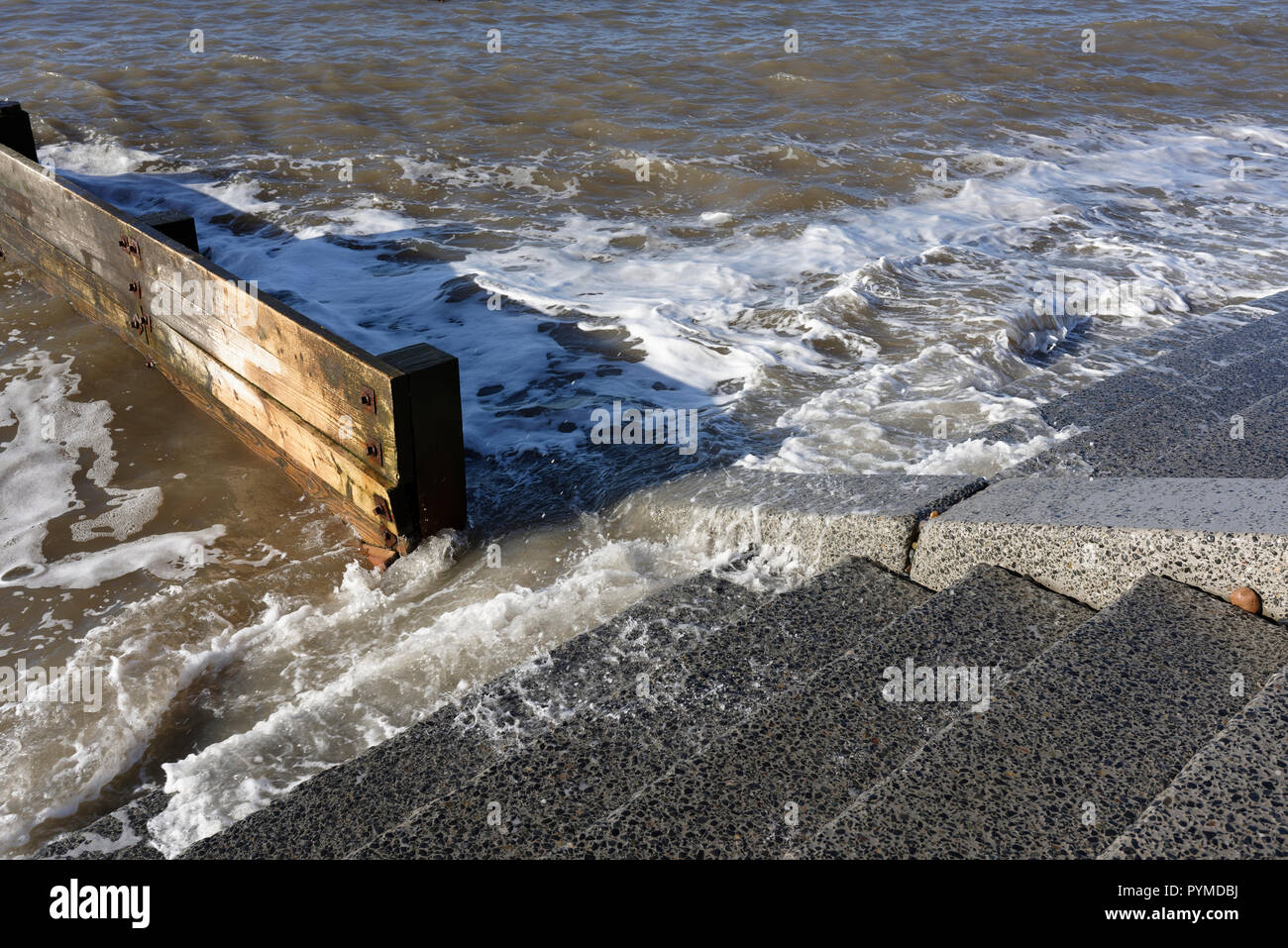 Waves breaking against timber groyne and concrete stepped revetment ...