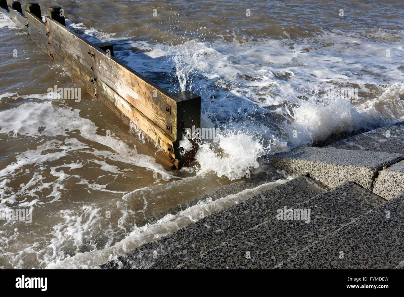 Waves breaking against timber groyne and concrete stepped revetment ...