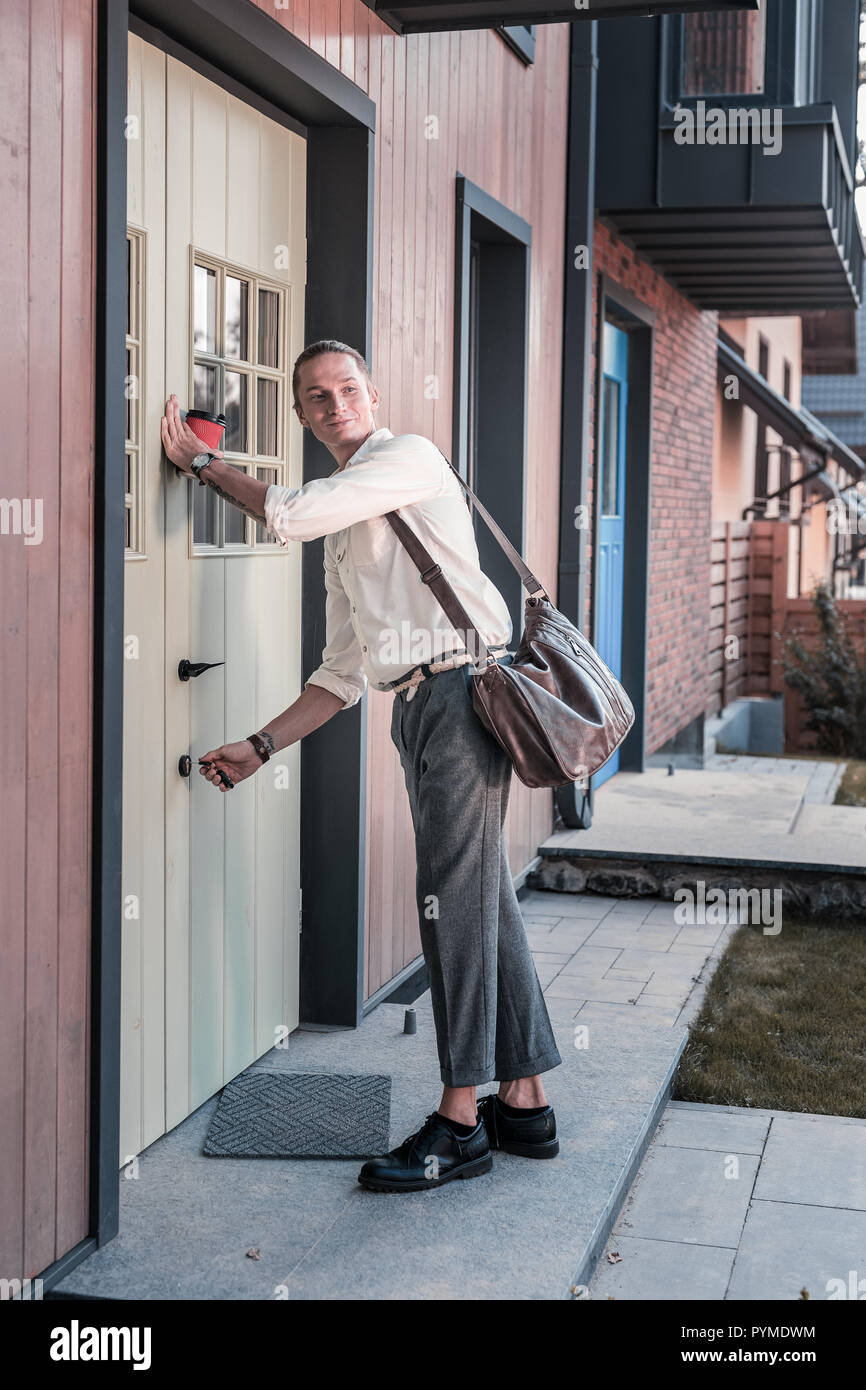 Pleasant handsome man closing his door while heading to the office ...