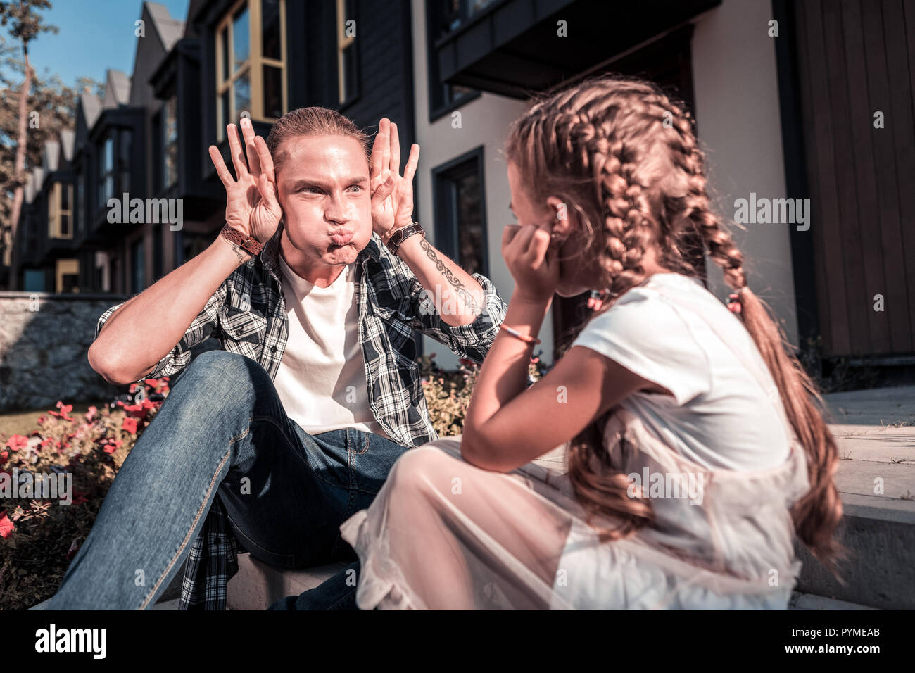Modern father making funny faces while entertaining his little daughter ...