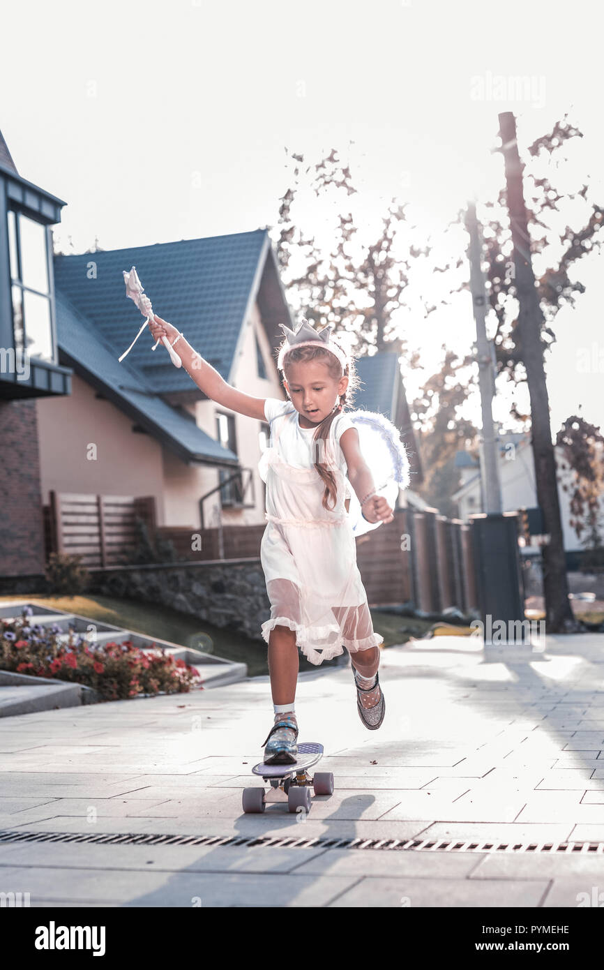 Modern little girl wearing little crown skateboarding near her house ...