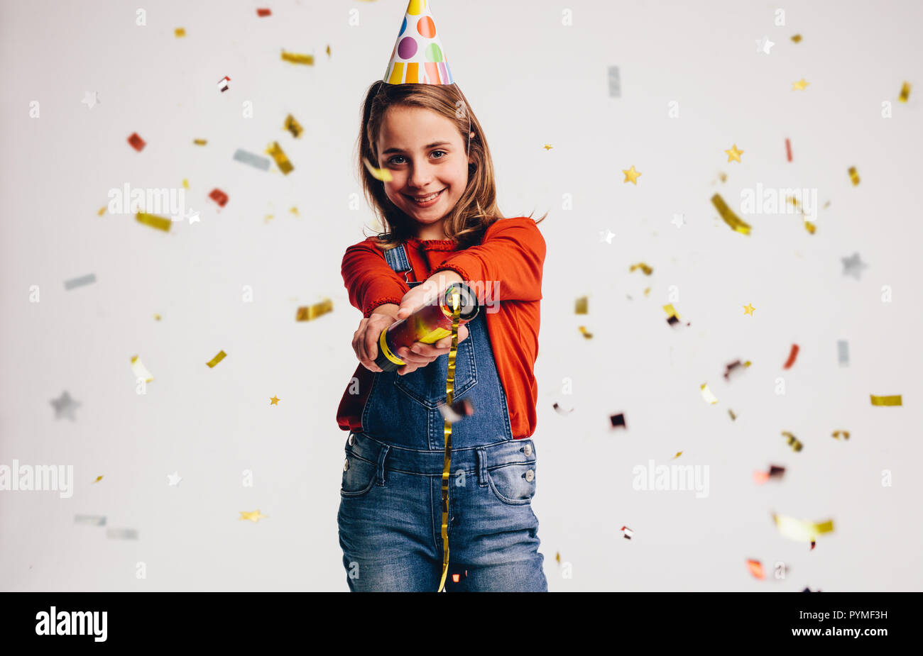 Portrait of girl holding a party popper with confetti flying all around ...