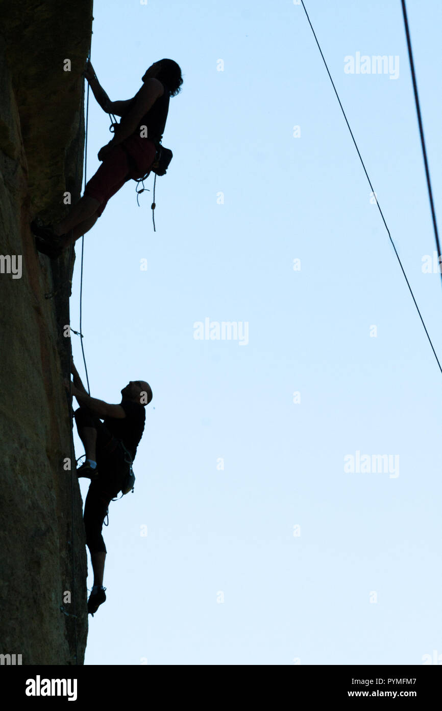 Back lit view of rock climbers climbing route at one side of the image ...