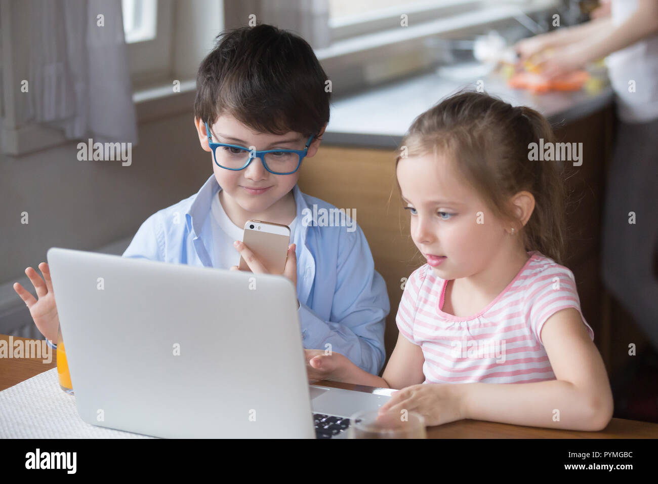 Adorable little kids using smartphone and laptop sitting indoors Stock ...