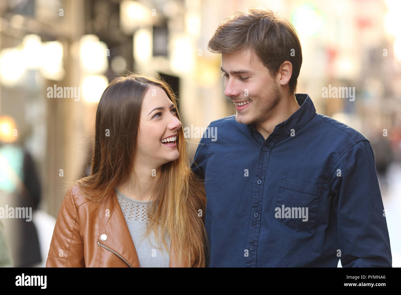 Front view of a happy couple walking and looking each other in the ...