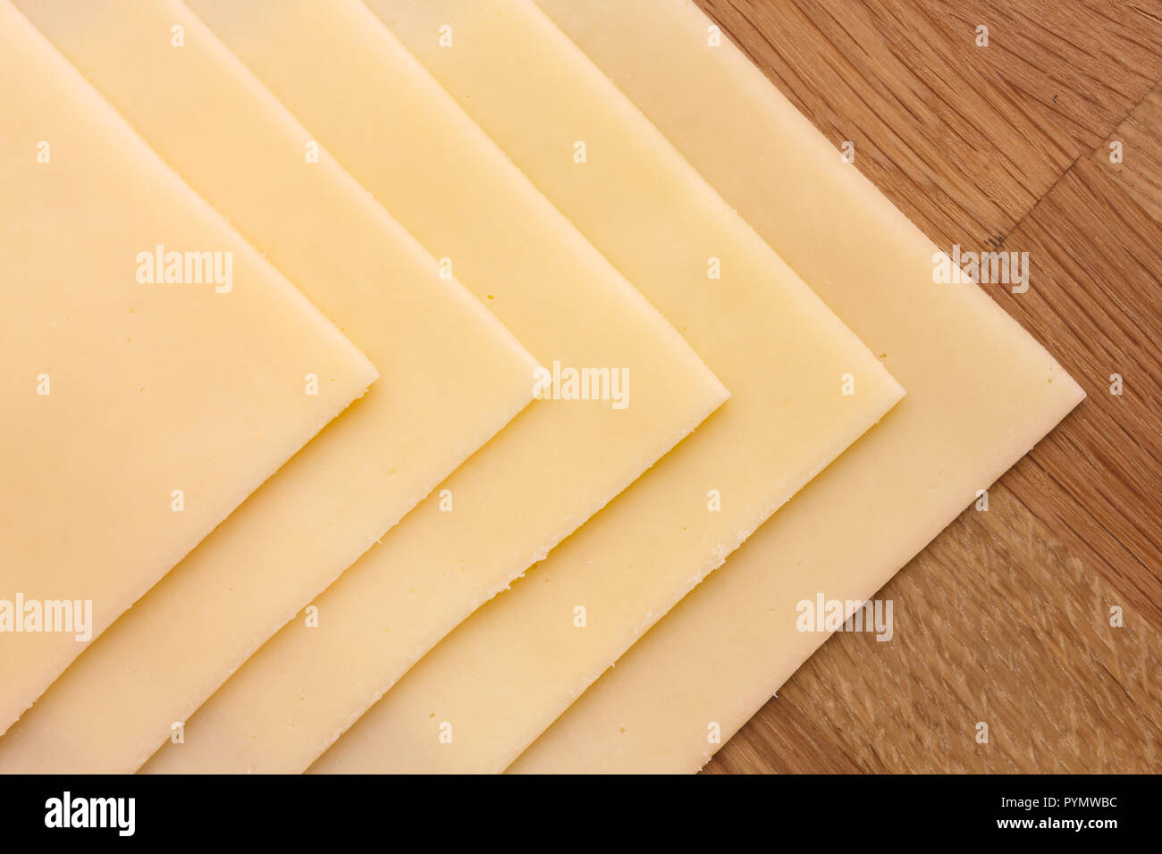 Sliced yellow sandwhich cheese neatly arranged on a wood surface. Shot ...