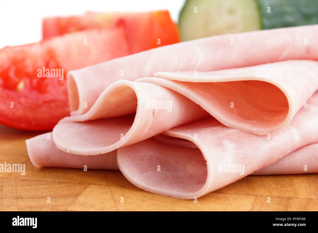 Processed ham randomly arranged on chopping board. Tomato and cucumber ...