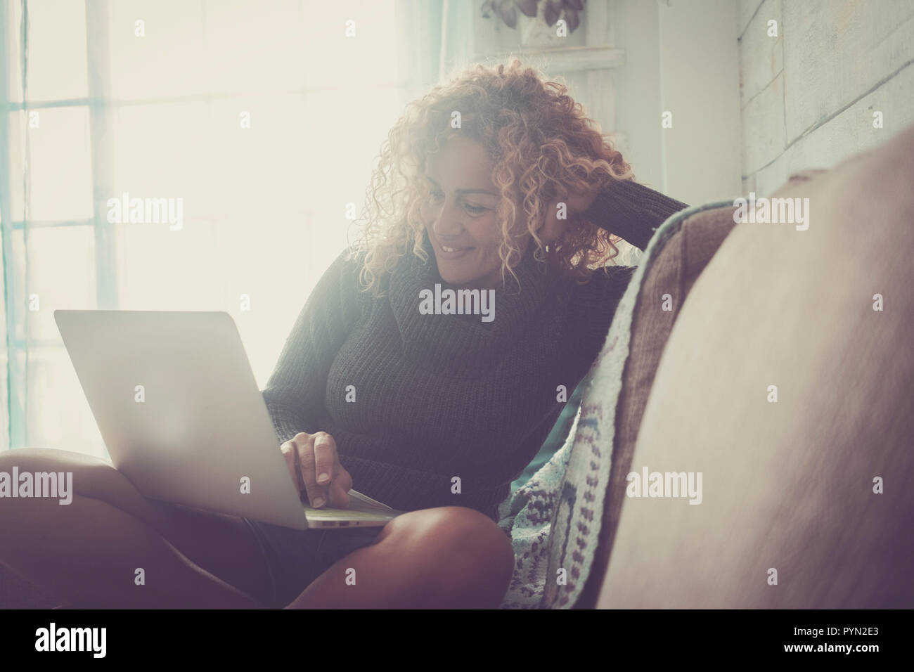 Curly woman with gray sweater sitting on brown sofa and blue blankets ...