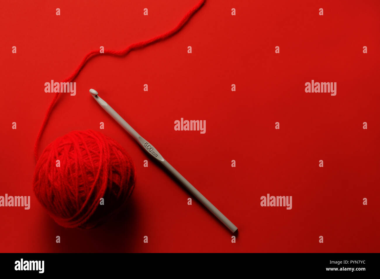 Red wool with crochet needle on red paper background Stock Photo - Alamy