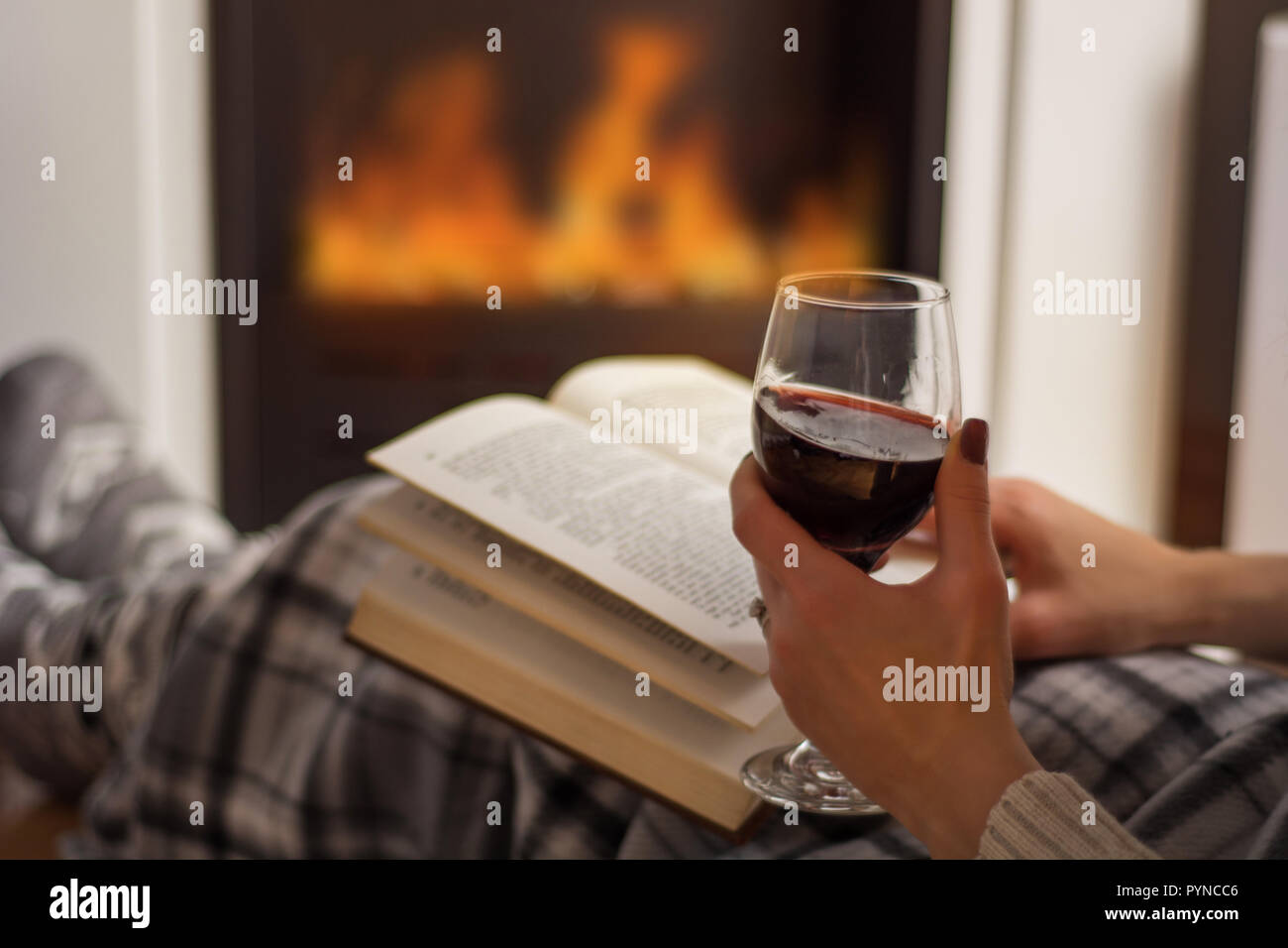 Woman reading book and drinking red wine in front of the fireplace ...