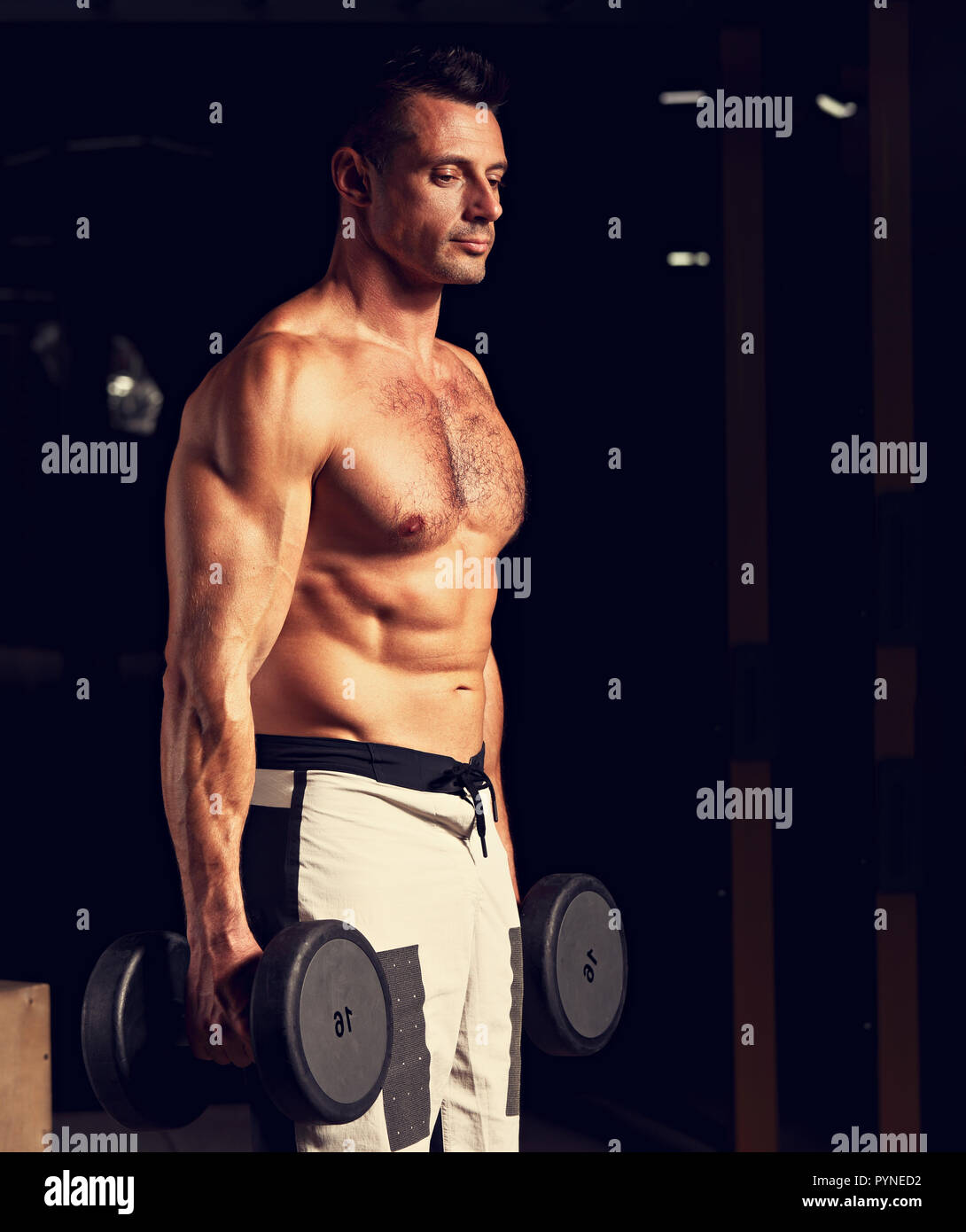 Handsome strong angry man doing the exercises with dumbbells on dark ...