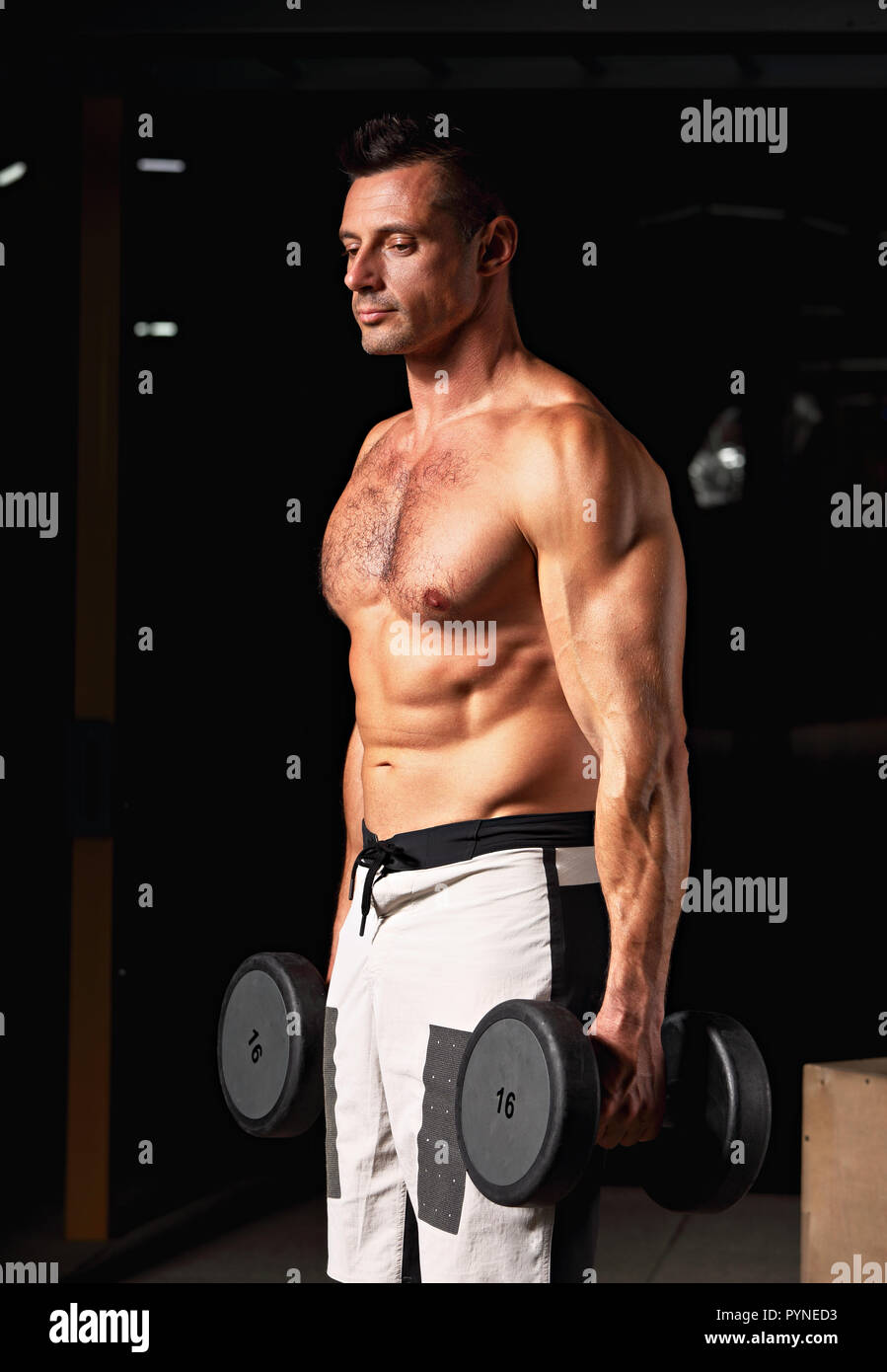 Handsome strong angry man doing the exercises with dumbbells on dark ...