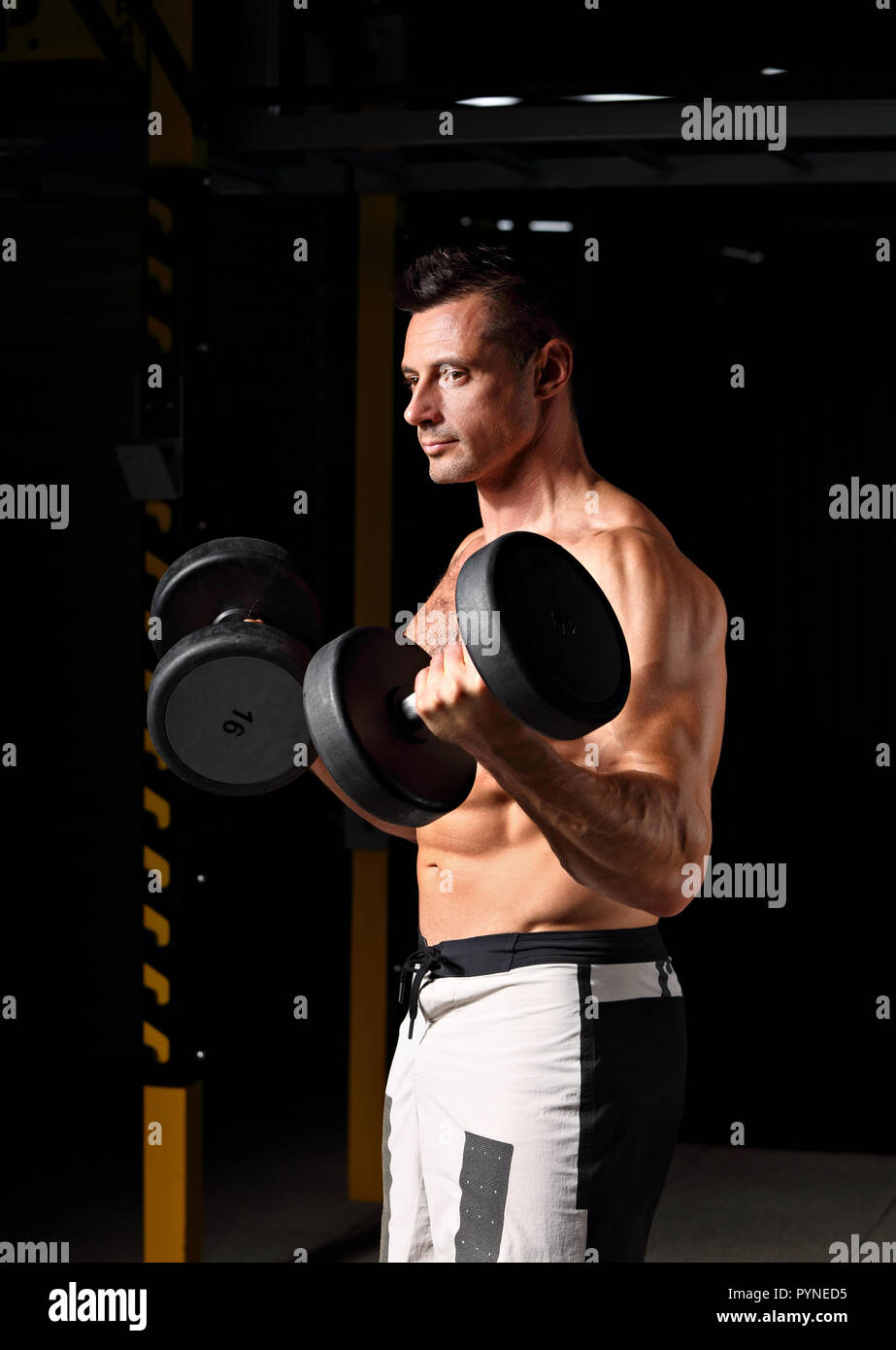 Handsome strong angry man doing the exercises with dumbbells on dark ...