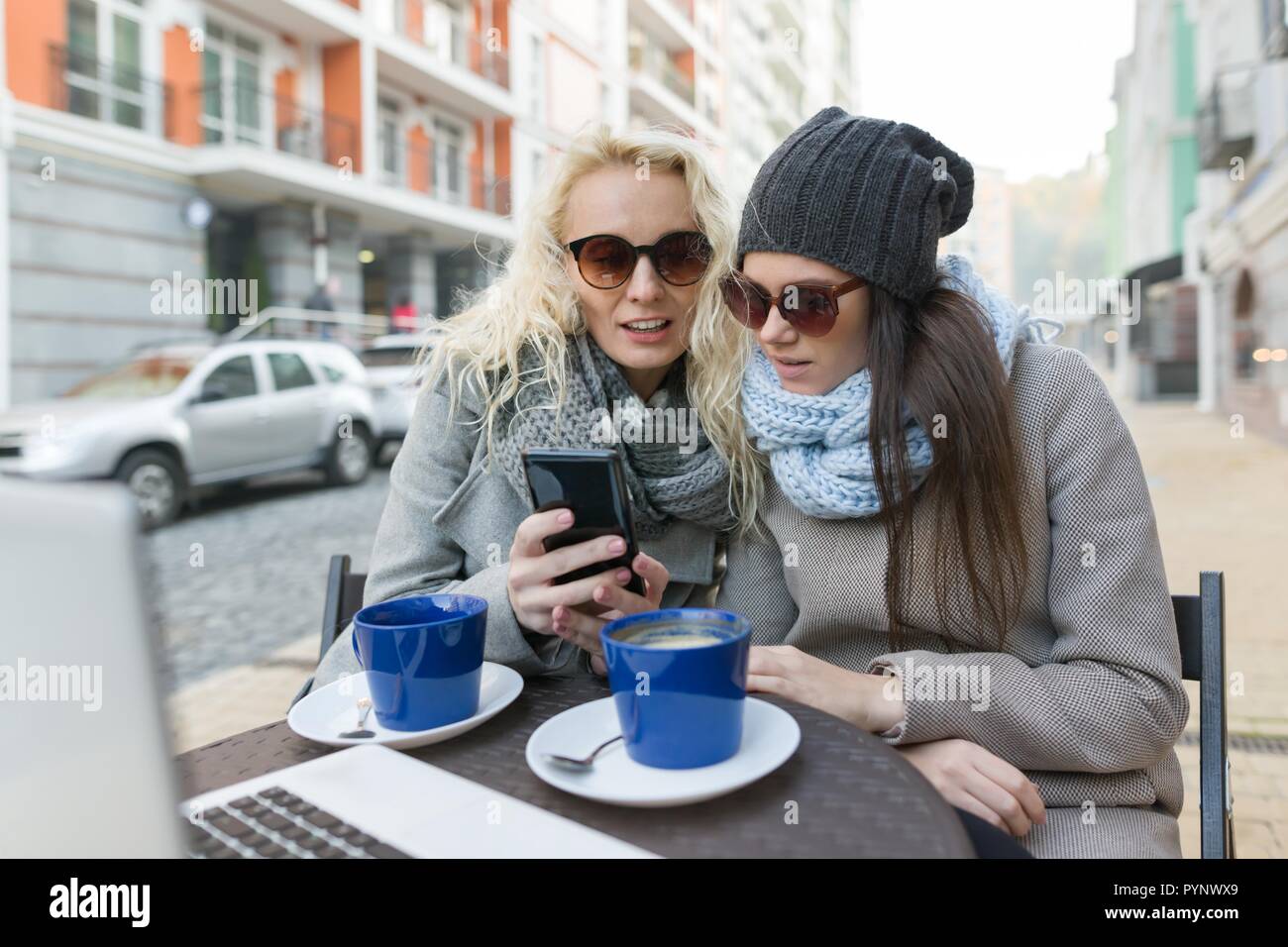 Autumn winter portrait of two young women in an outdoor cafe, drinking ...