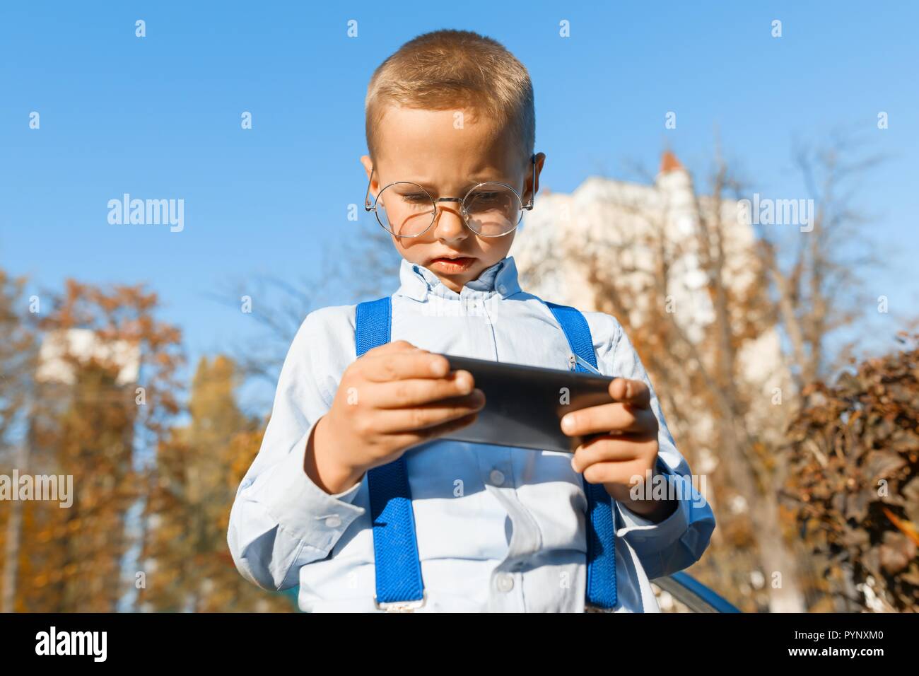 Smart boy in glasses with a mobile phone. A child in a classic shirt in ...