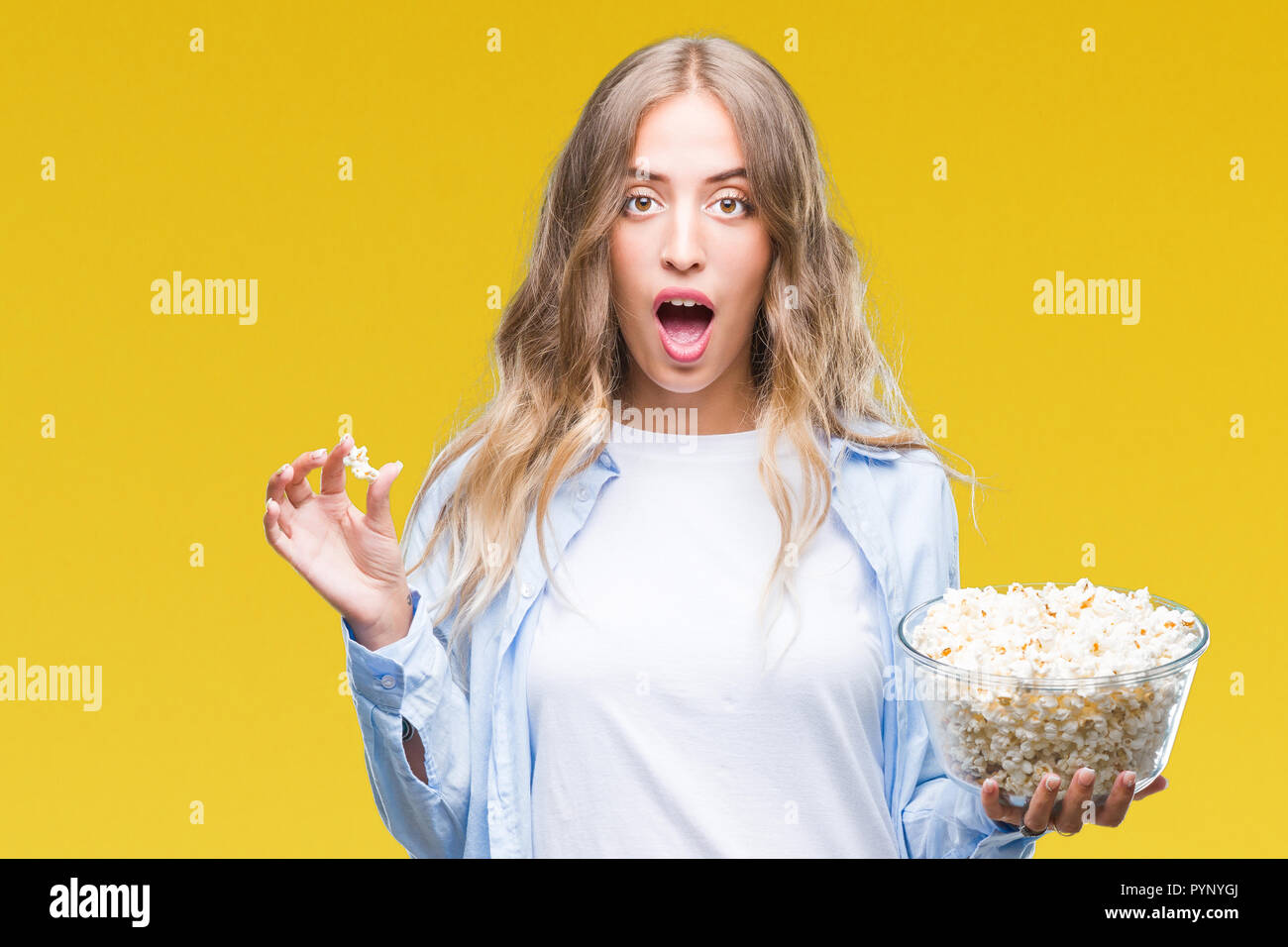 Beautiful young blonde woman eating popcorn over isolated background ...