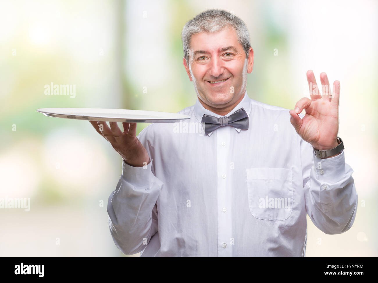 Handsome senior waiter man holding silver tray over isolated background ...