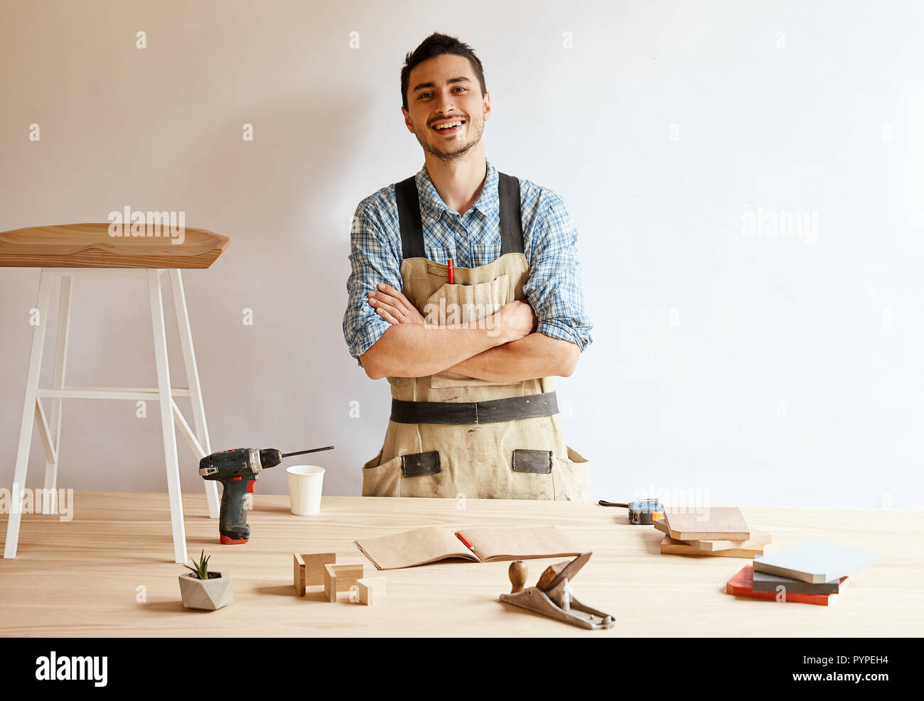 Confident young woodworker standing next to workbench in his carpentry ...