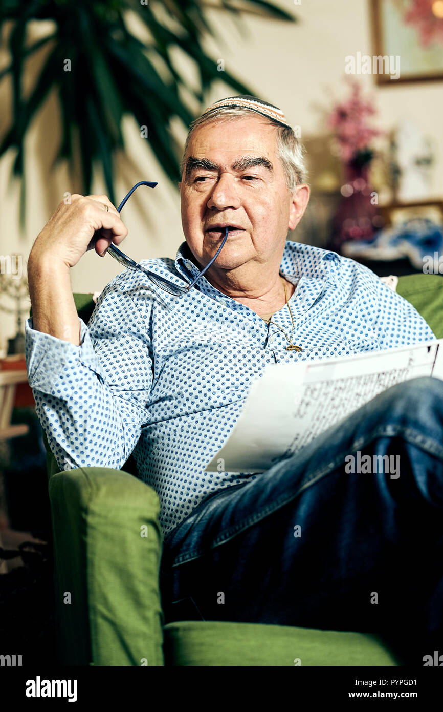 Jewish senior with glasses sitting in the armchair reading a torah book ...