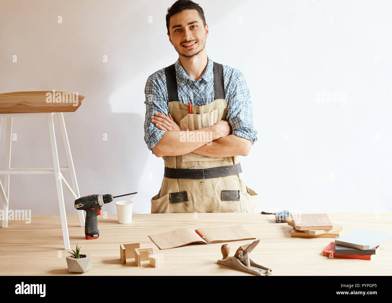 Confident young woodworker standing next to workbench in his carpentry ...