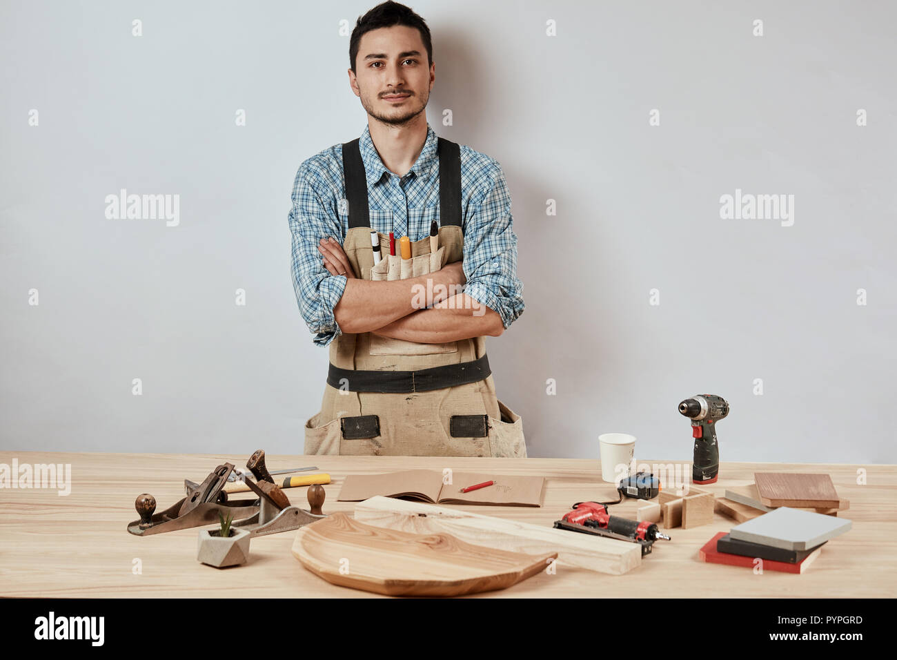 Confident young woodworker standing next to workbench in his carpentry ...