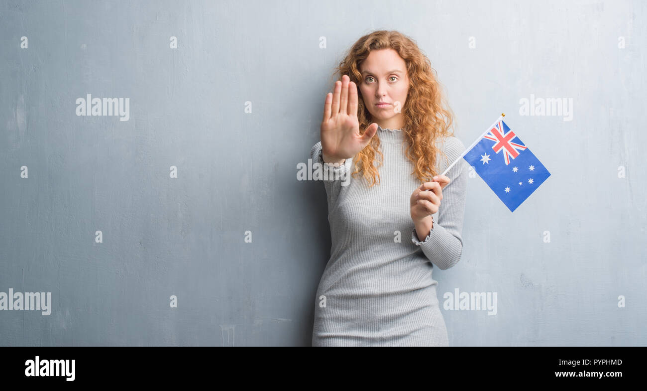 Young redhead woman over grey grunge wall holding flag of Australia ...