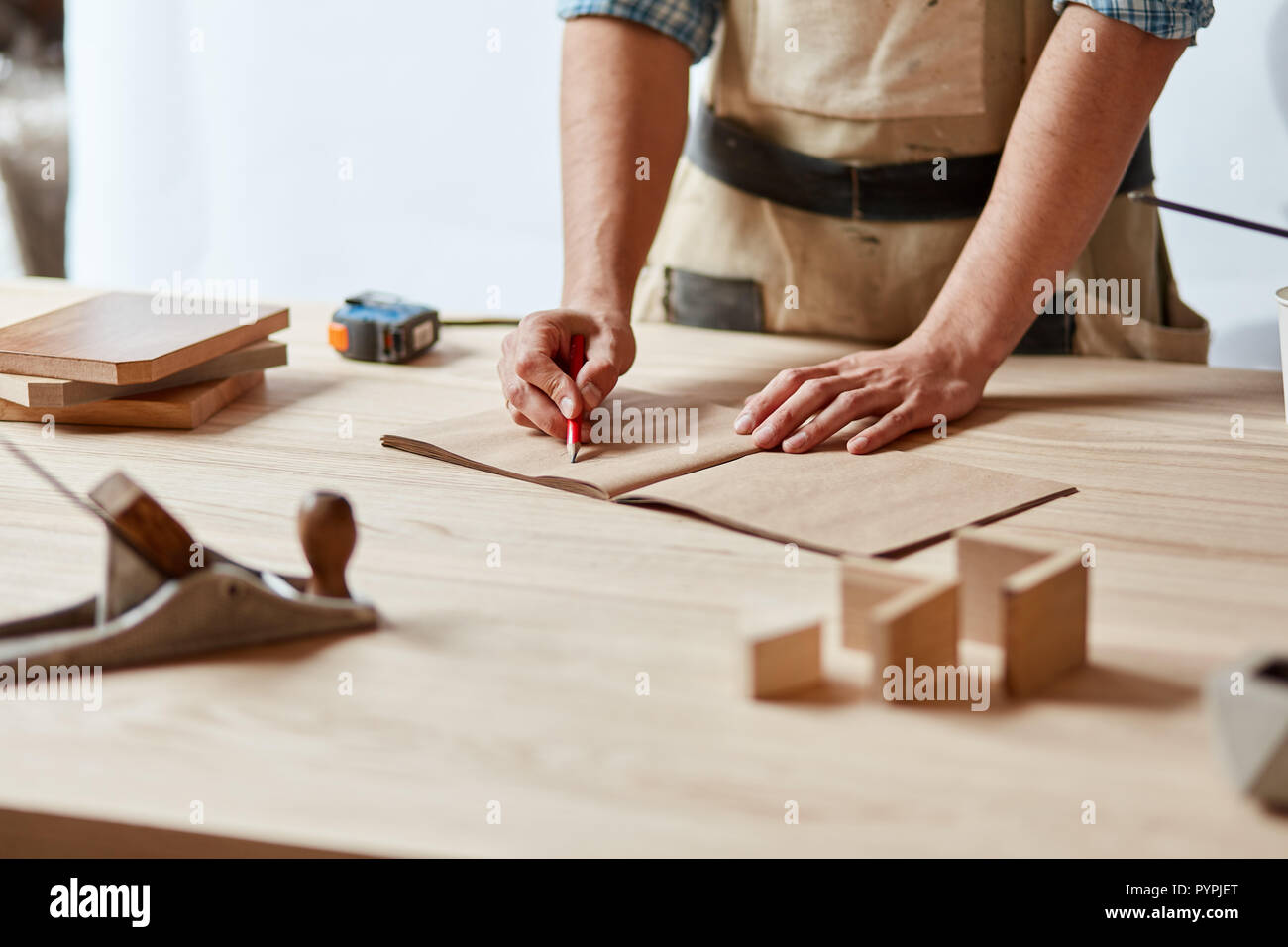 Closeup view of a carpenter using a red pencil to draw a line on a ...