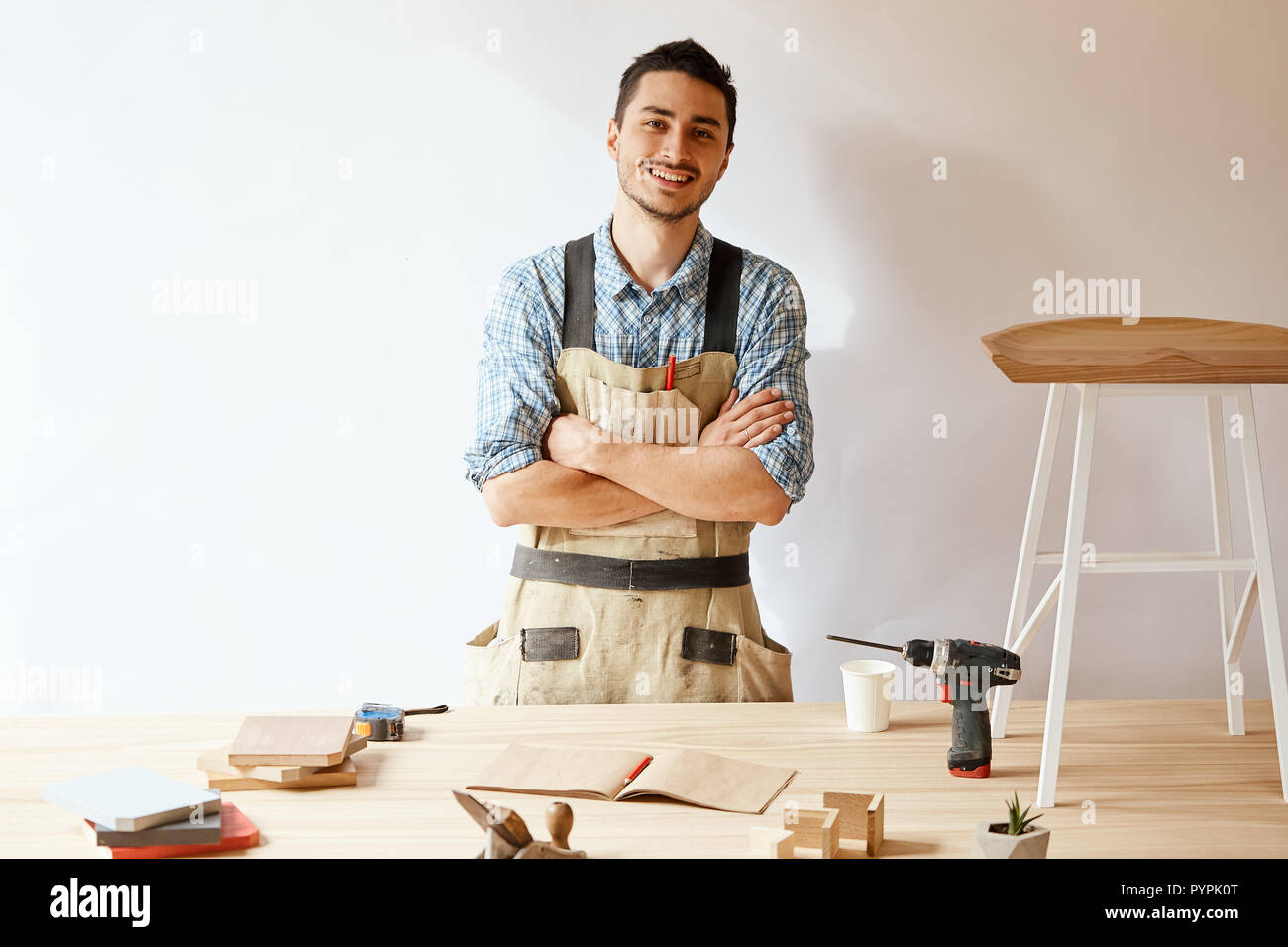 Confident young woodworker standing next to workbench in his carpentry ...