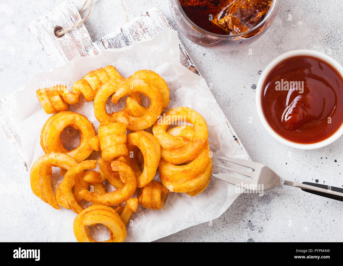 Curly fries fast food snack on wooden board with ketchup and glass of ...