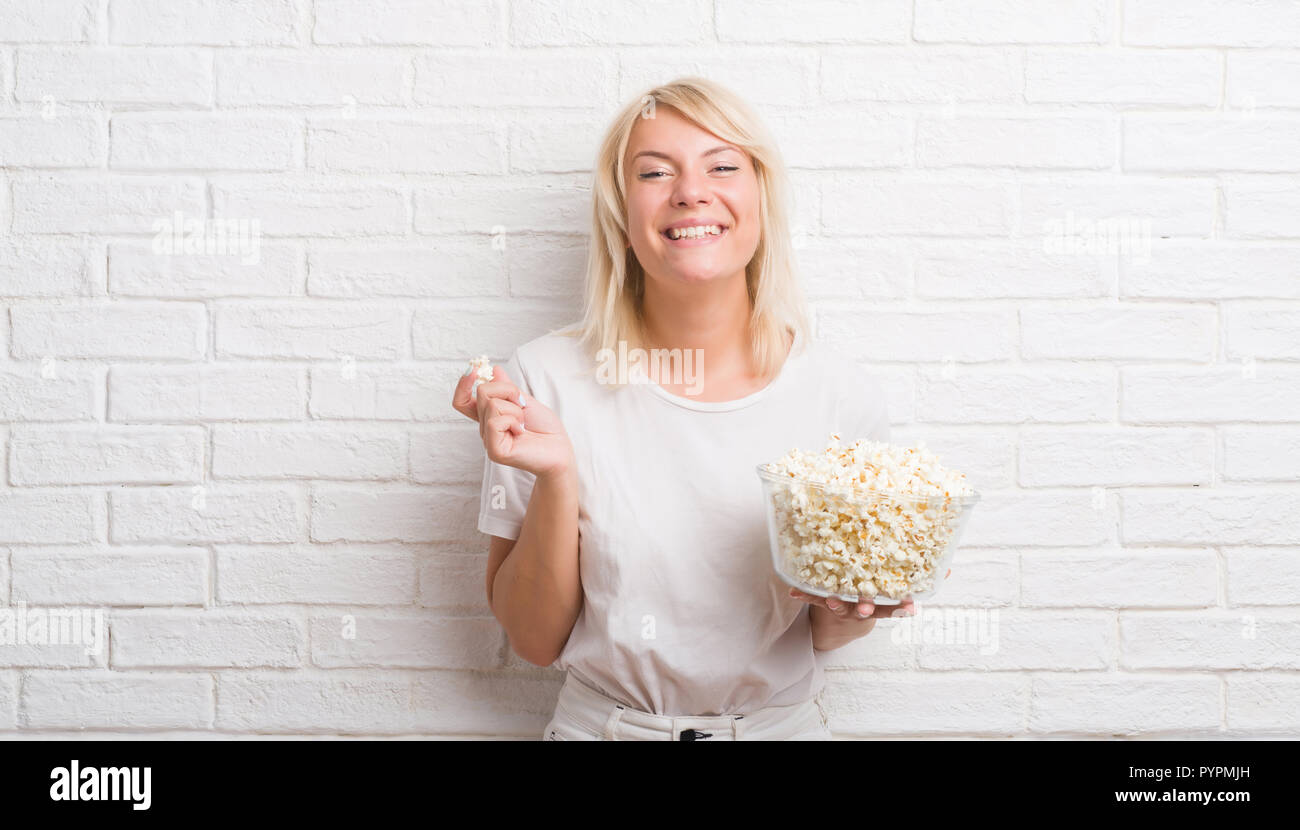 Adult caucasian woman over white brick wall eating pop corn with a ...