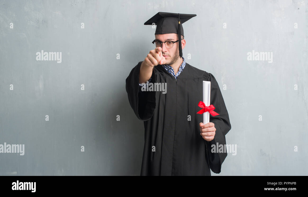Young caucasian man over grey grunge wall wearing graduate uniform ...