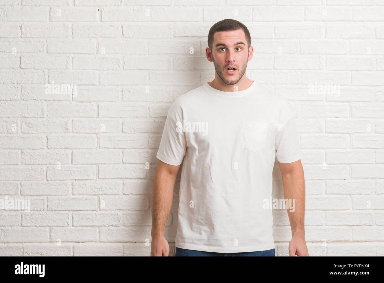 Young caucasian man standing over white brick wall afraid and shocked ...