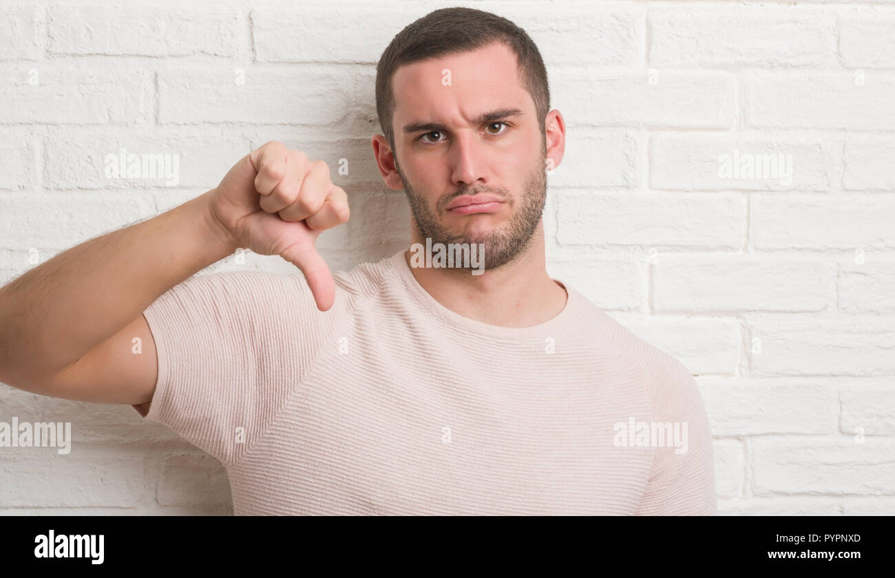 Young caucasian man standing over white brick wall with angry face ...