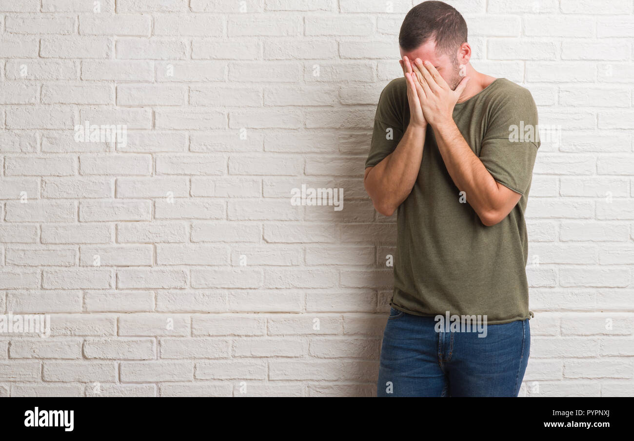 Young caucasian man standing over white brick wall with sad expression ...