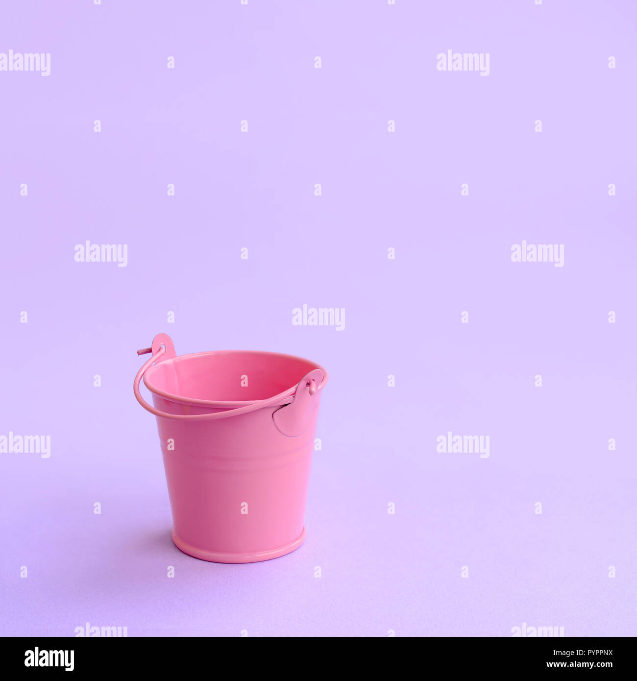 A miniature empty pink bucket lies on a violet pastel background ...