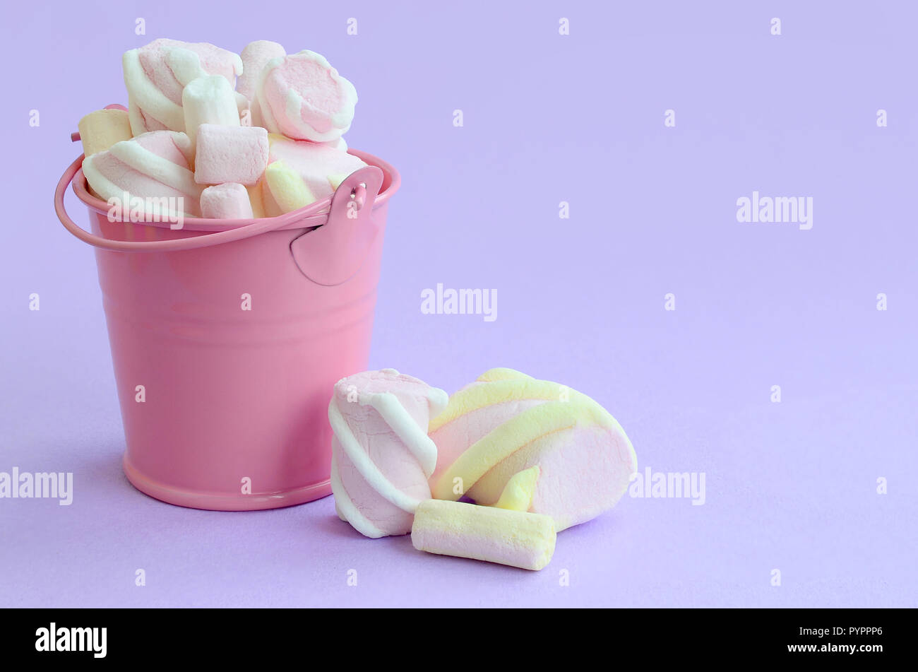 A miniature pink bucket filled with marshmallow lies on a violet pastel ...