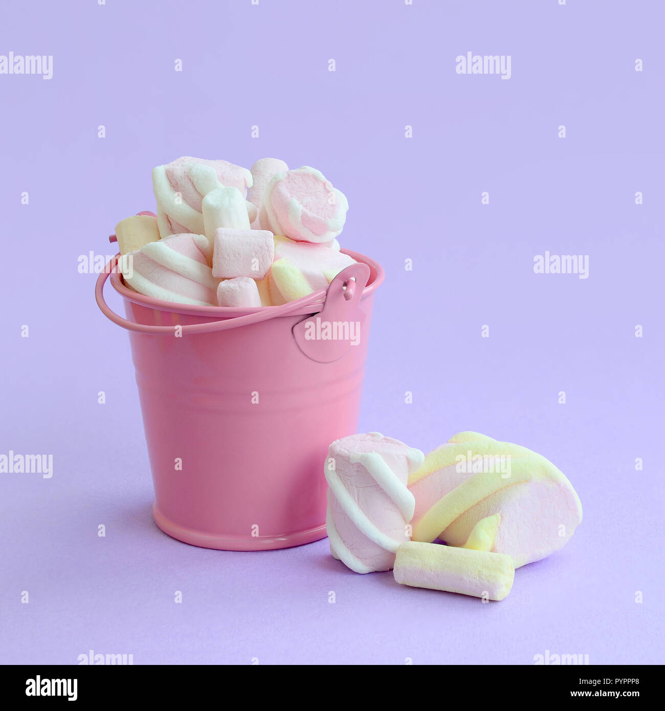 A miniature pink bucket filled with marshmallow lies on a violet pastel ...