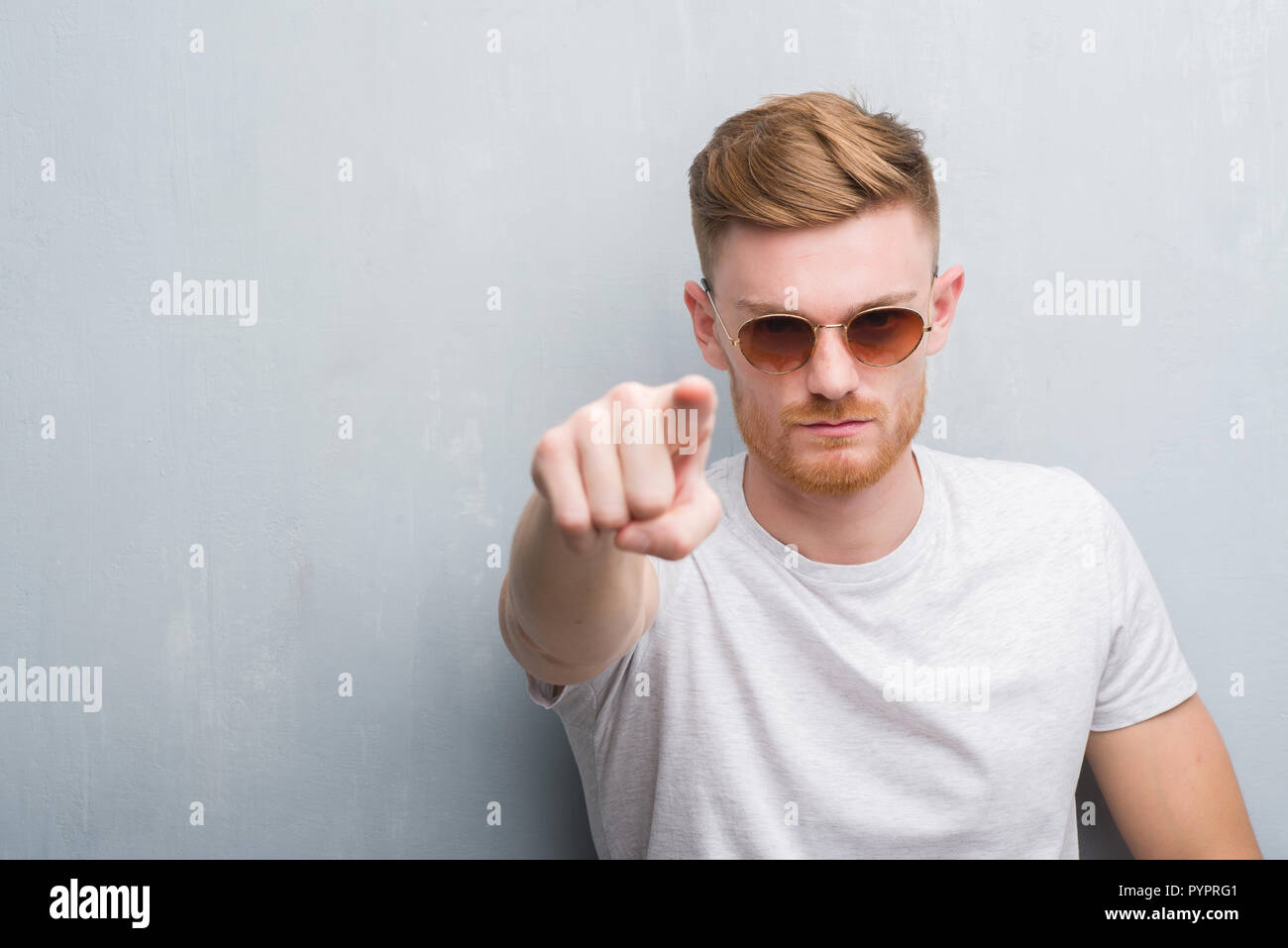 Young redhead man over grey grunge wall wearing retro sunglasses ...
