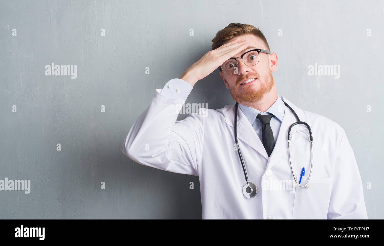 Young redhead doctor man over grey grunge wall stressed with hand on ...