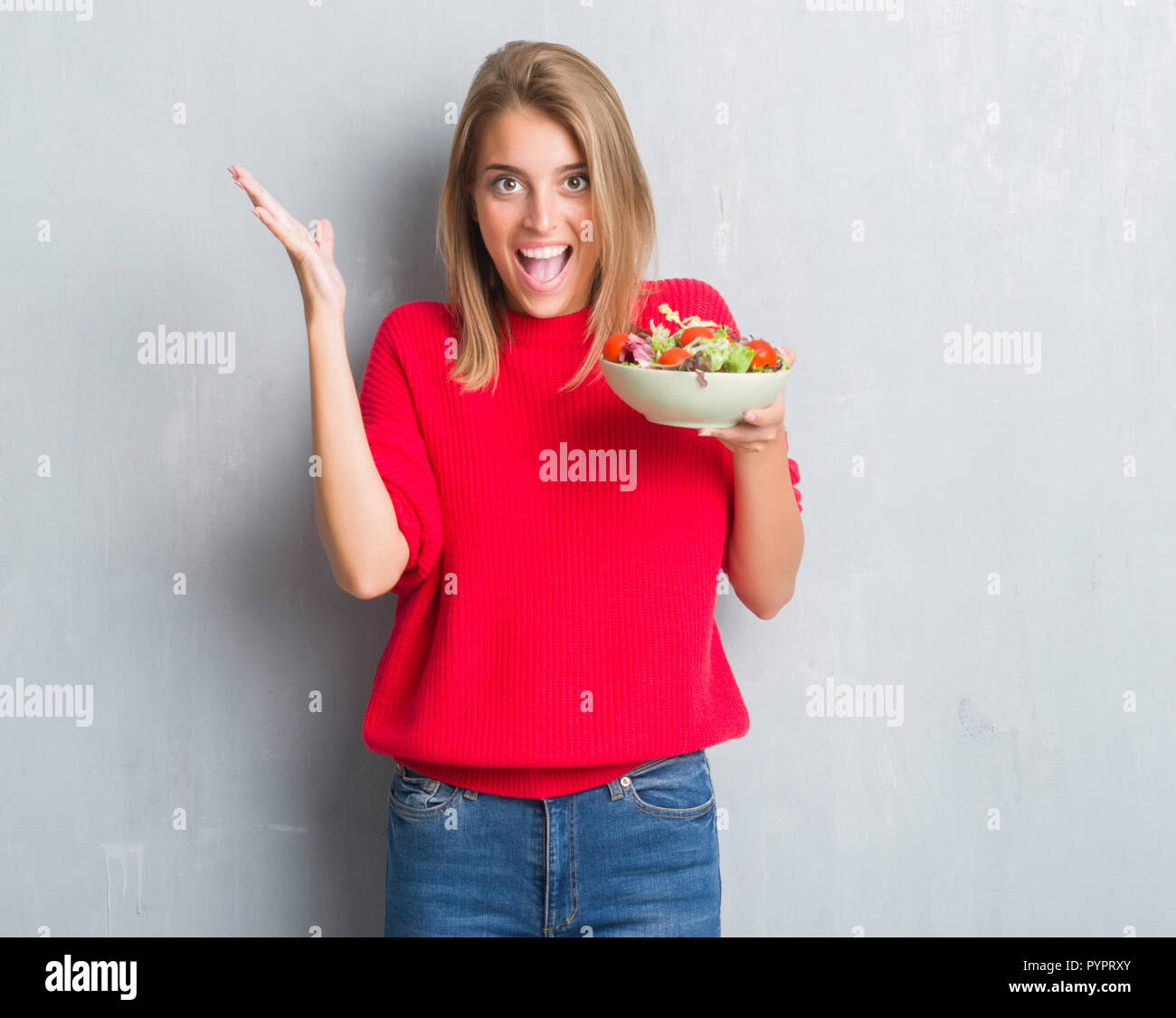 Beautiful young woman over grunge grey wall eating tomato salad very ...
