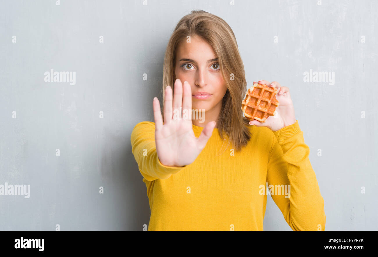Beautiful young woman over grunge grey wall eating waffle with open ...