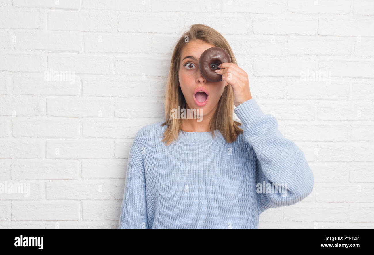 Beautiful young woman over white brick wall eating chocolate donut ...