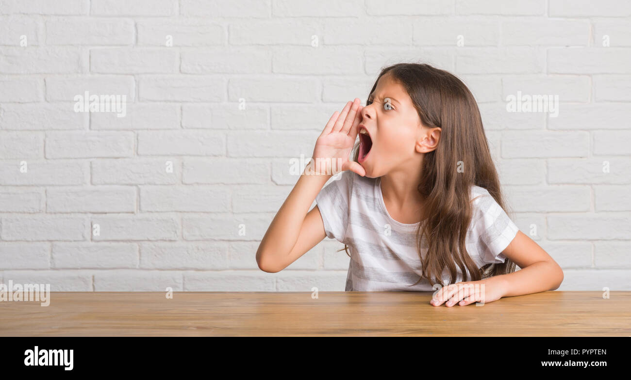 Young hispanic kid sitting on the table at home shouting and screaming ...