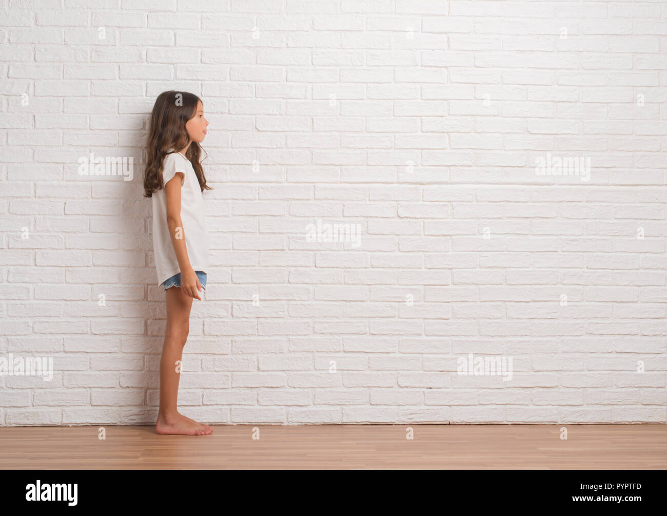 Young hispanic kid stading over white brick wall looking to side, relax ...