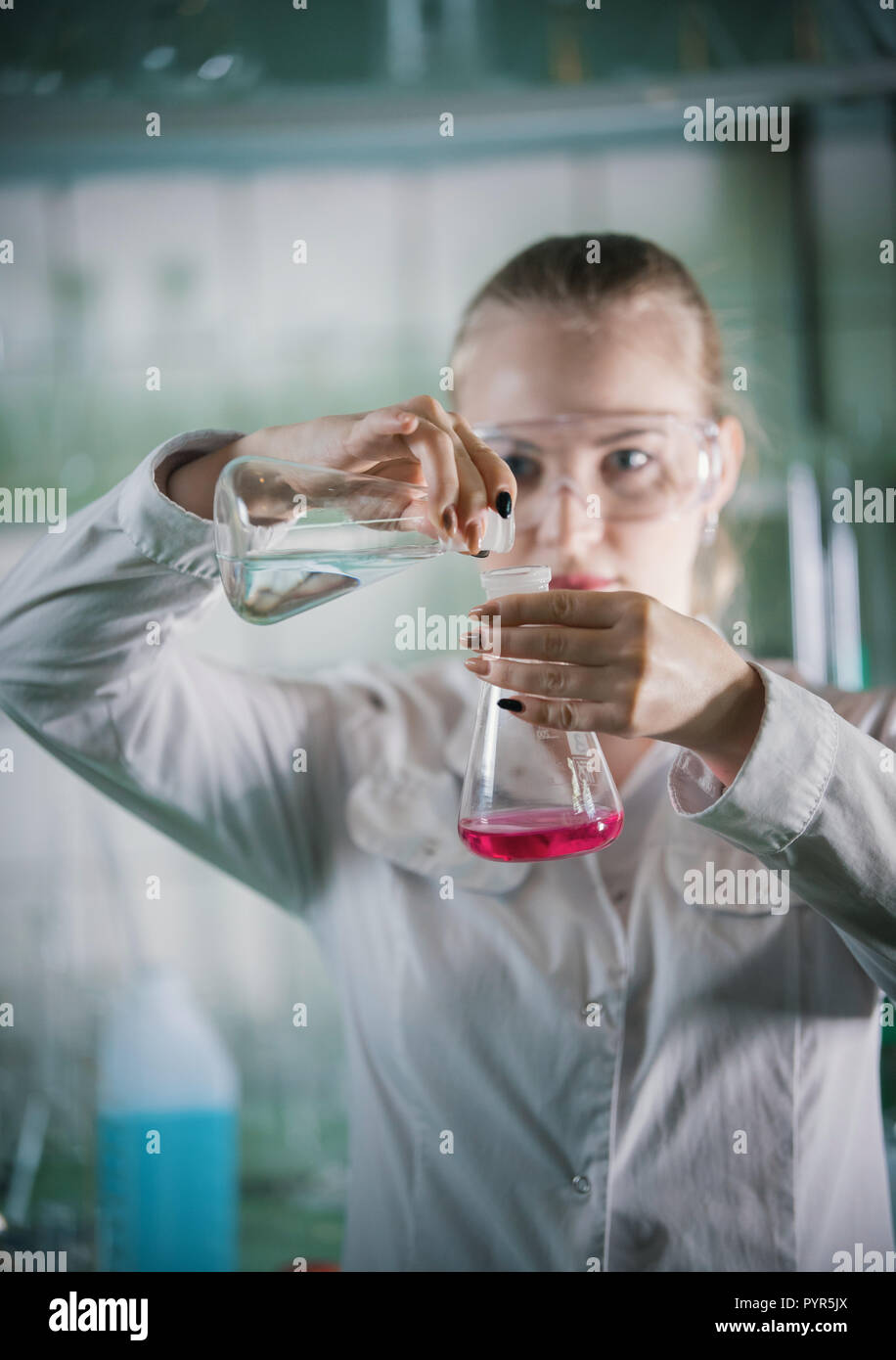 Chemical laboratory. Young blonde woman holding two flasks with liquid ...