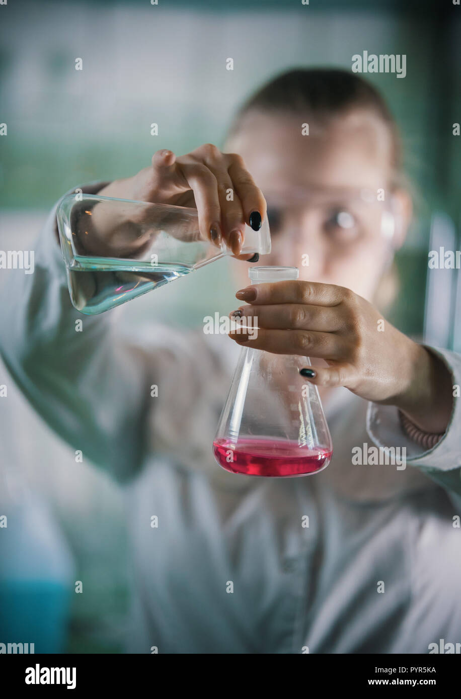 Chemical laboratory. Young blonde woman holding two flasks with liquid ...
